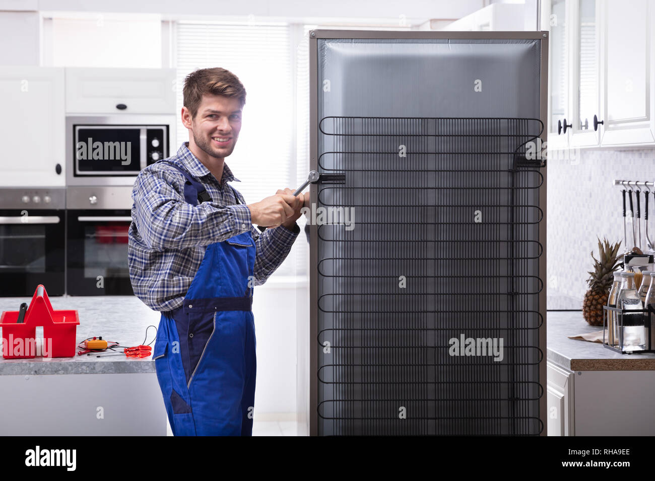 Serviceman In Overall Working On Fridge With Wrench In Kitchen Stock ...