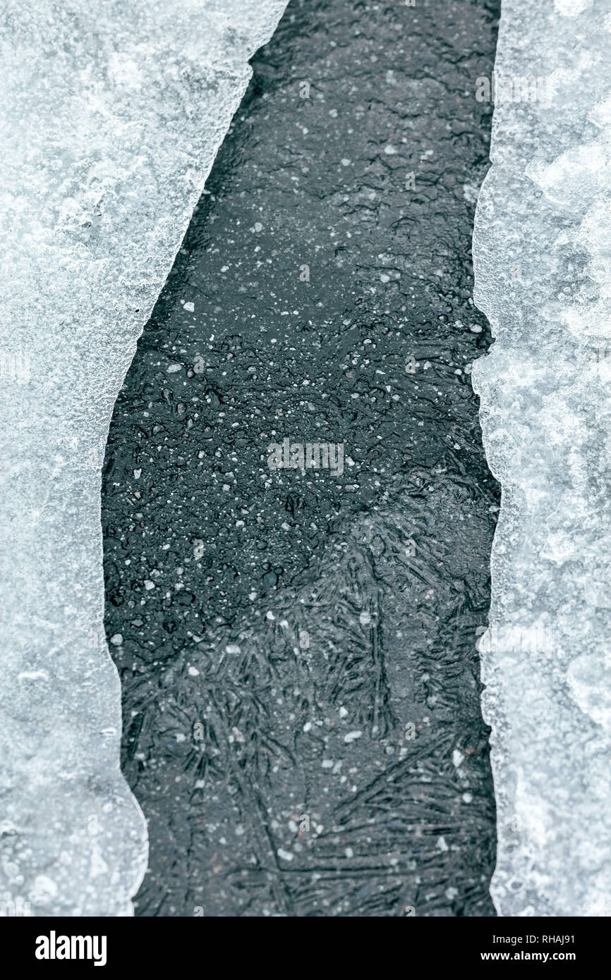 frozen black asphalt road surface with melting ice. spring natural ...