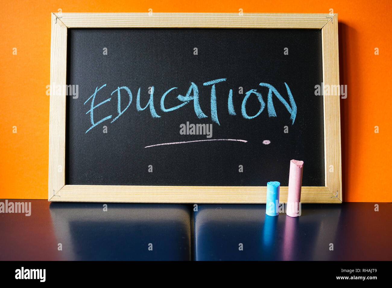 Black board on orange background with text Education written in chalk ...