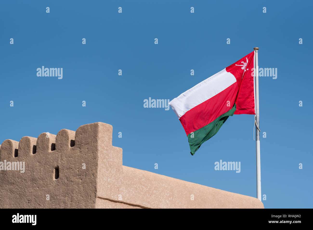 National flag of Oman flying from pole on top of old fort close to ...
