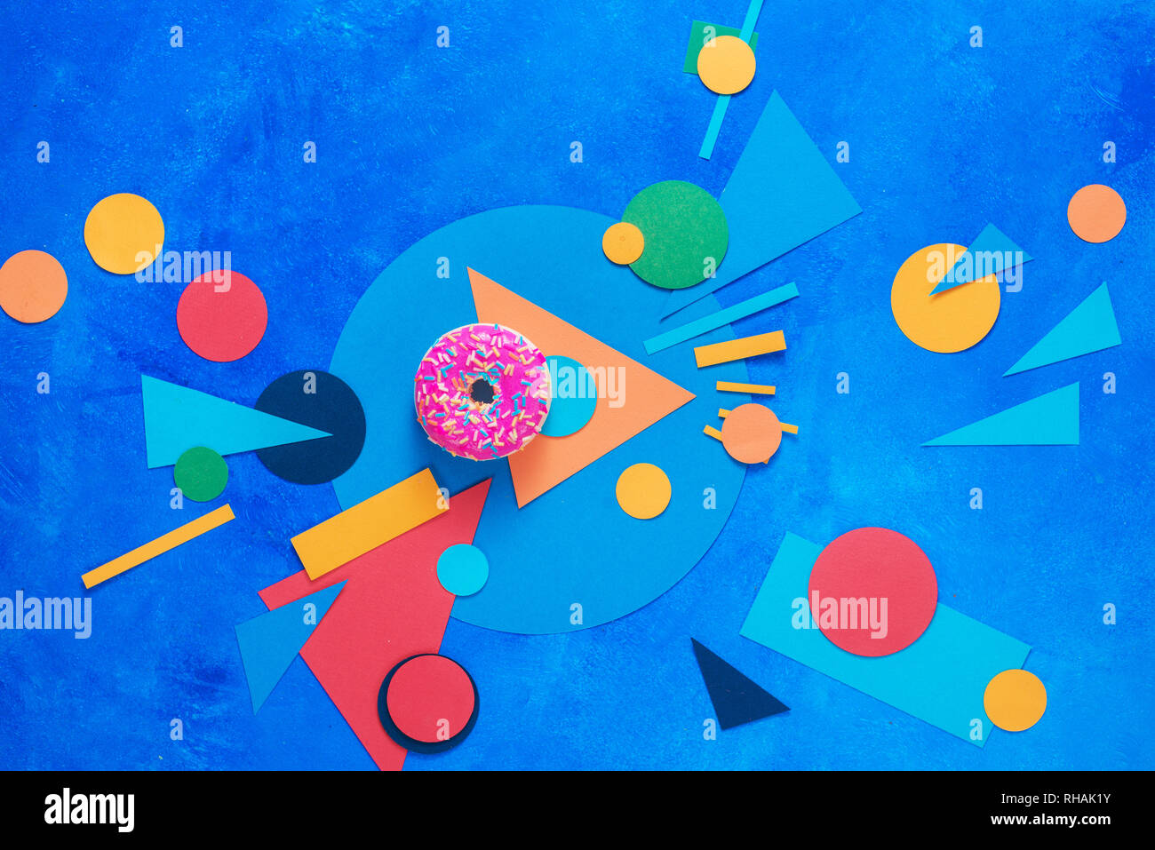 A pink donut with colorful paper decorations. Color blocking flat lay ...