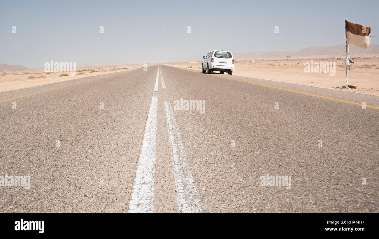 Asphalt road straight in the desert in the south of Oman with a parked ...