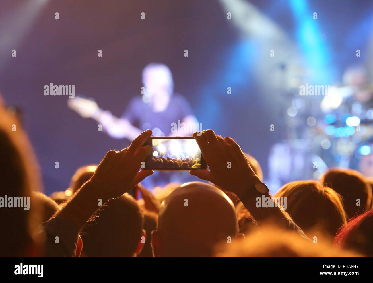 fan photographs a bassist during a rock concert using a modern ...