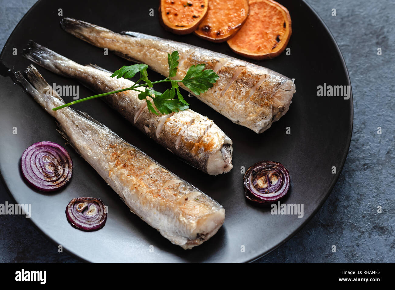 Fried hake served with sweet potatoes and red onion Stock Photo - Alamy
