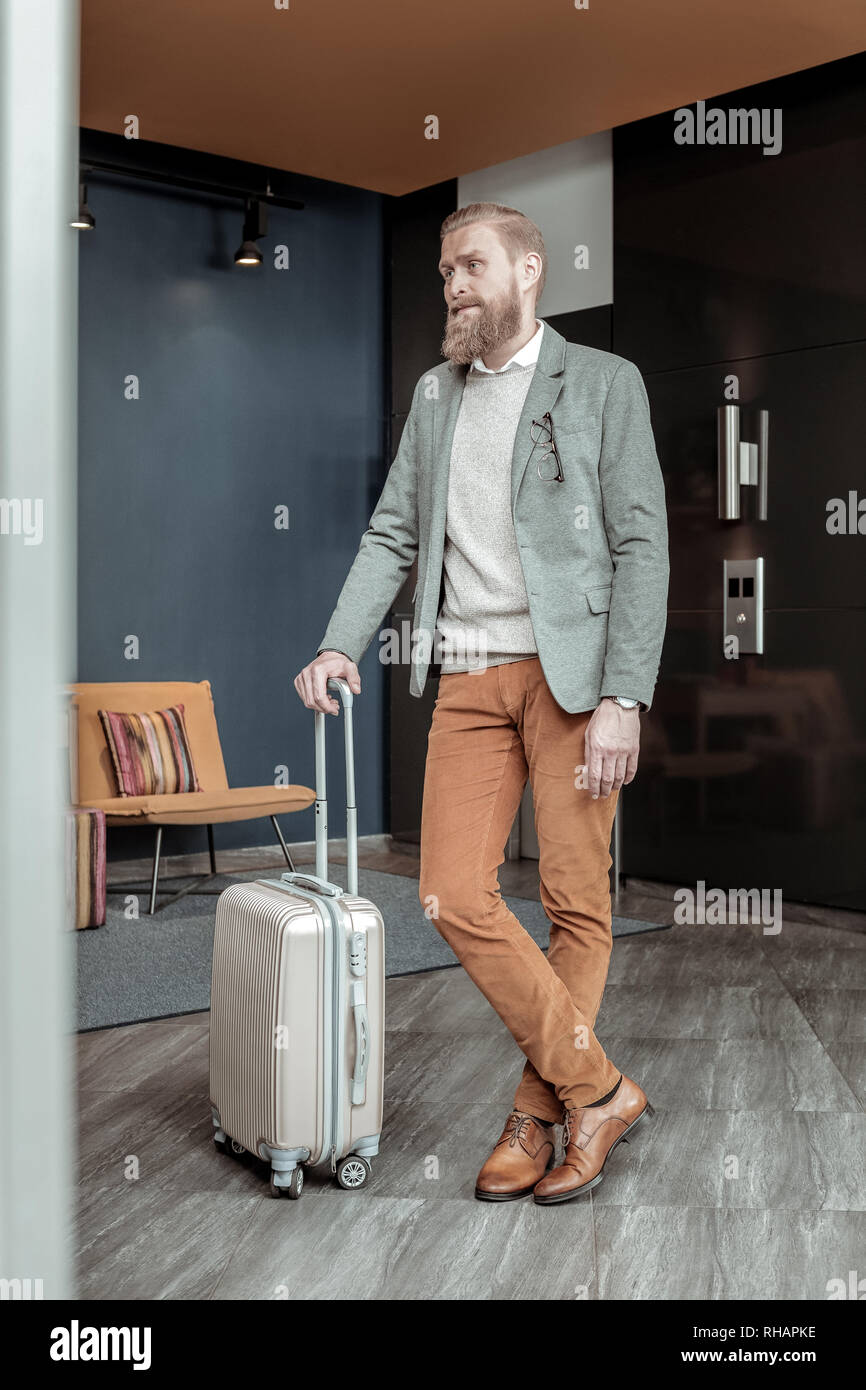 Waiting for you. Pleased man crossing his legs while leaning on case ...