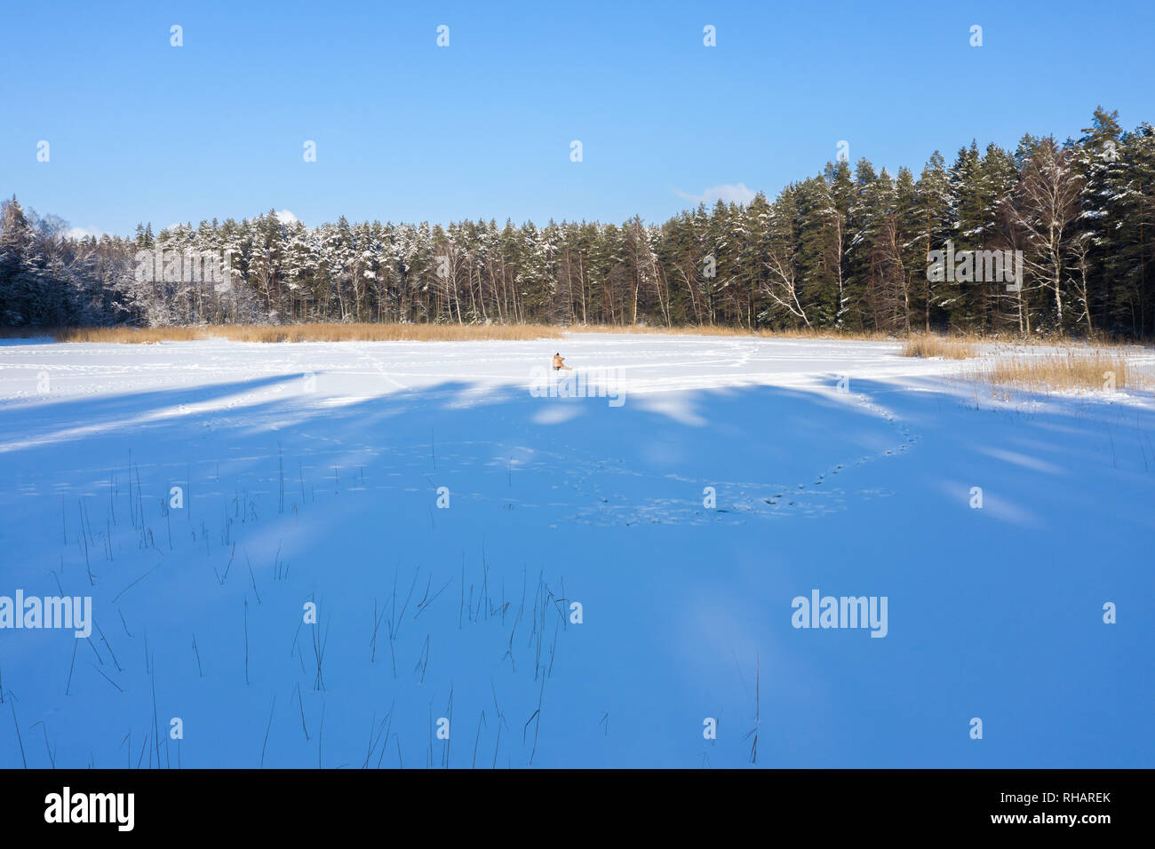 Aerial view over frozen lake cover in white snow with long blue shadows ...