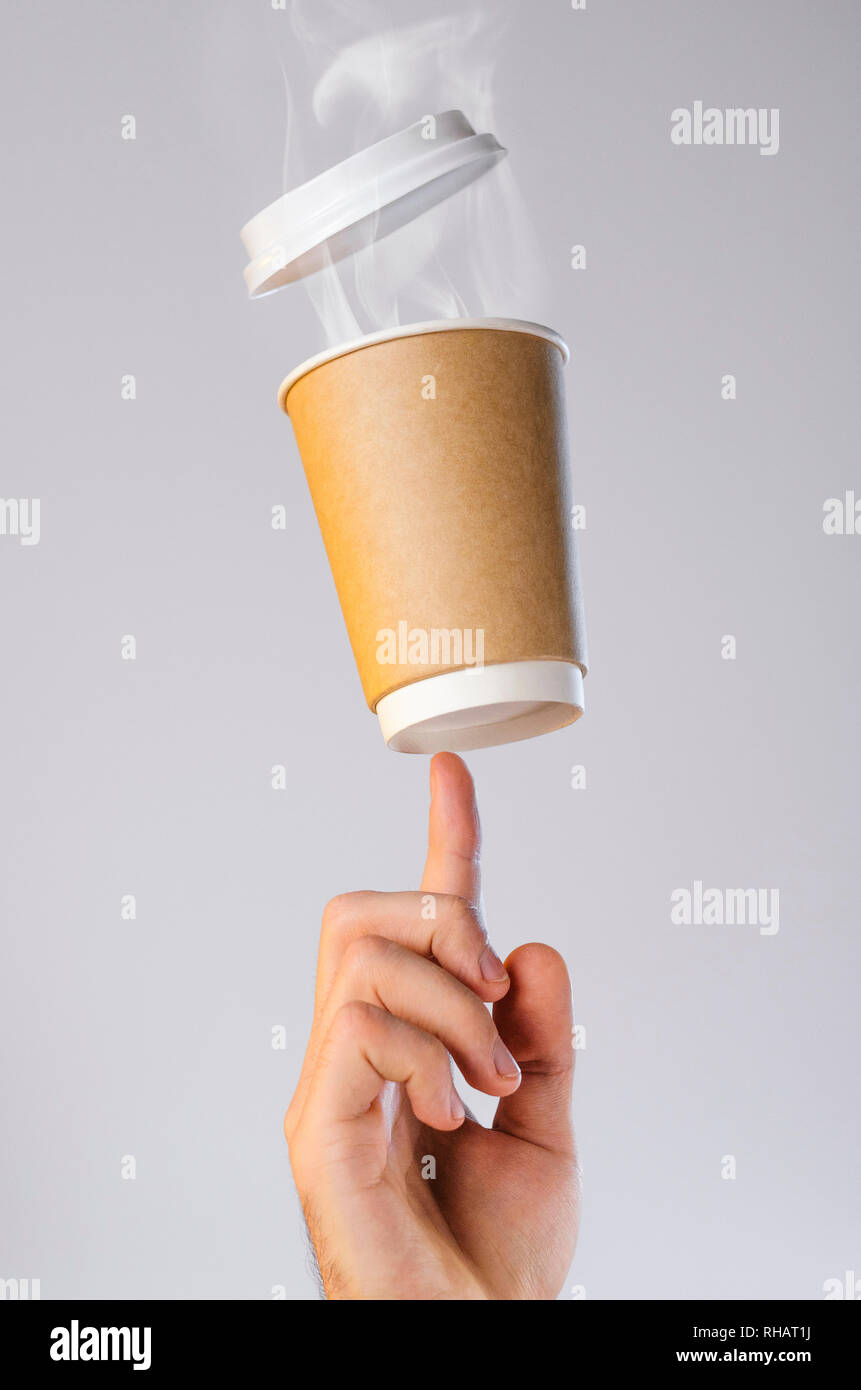 A paper cup with hot coffee and a cloud of vapor balances at the tip of ...