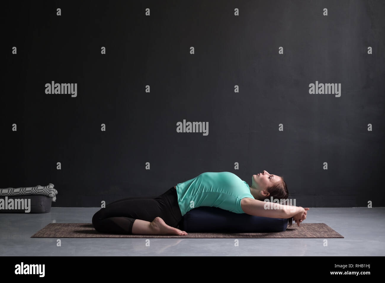 Beautiful athletic girl doing yoga supta virasana asana using bolster ...