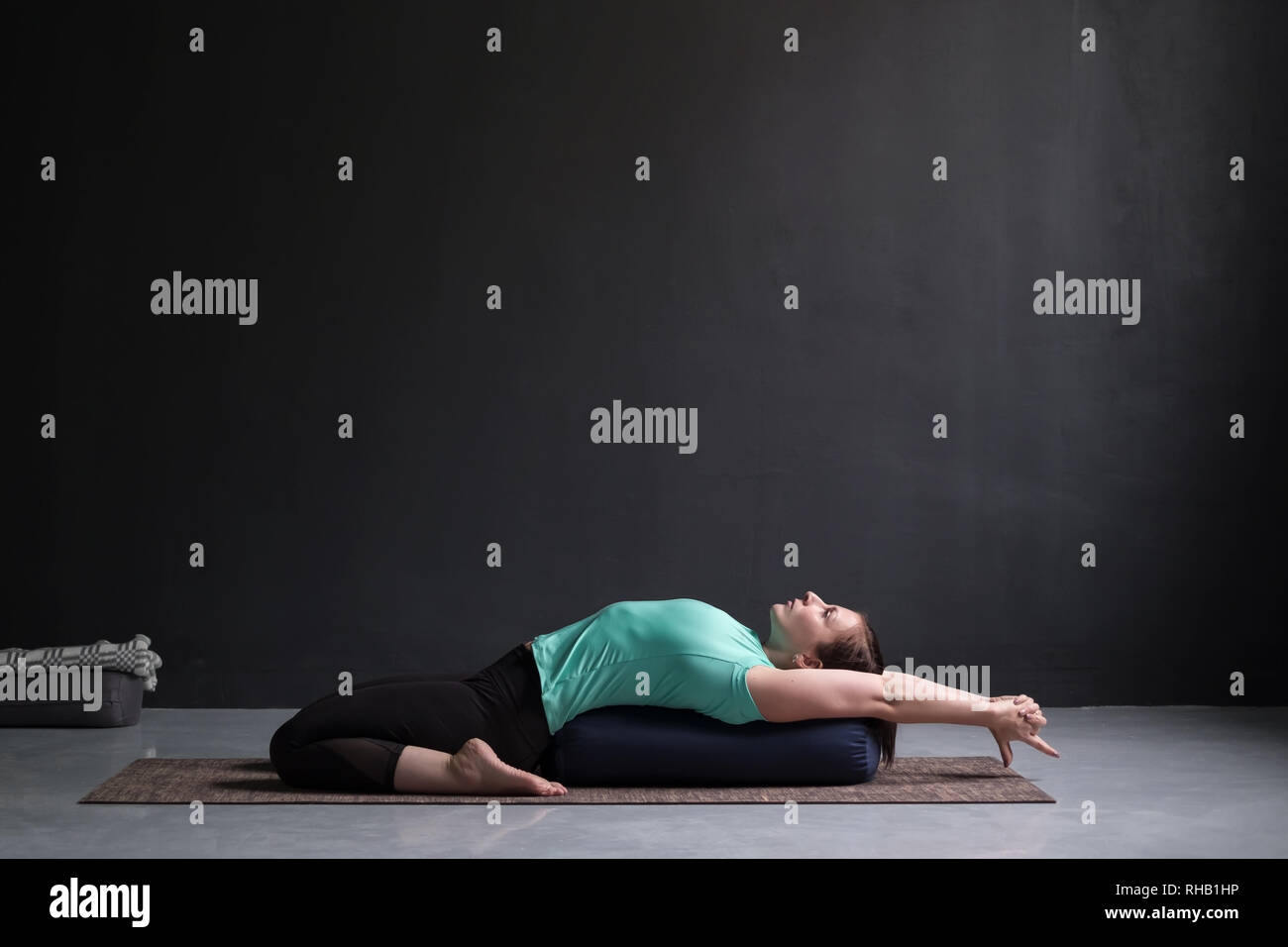 Beautiful athletic girl doing yoga supta virasana asana using bolster ...