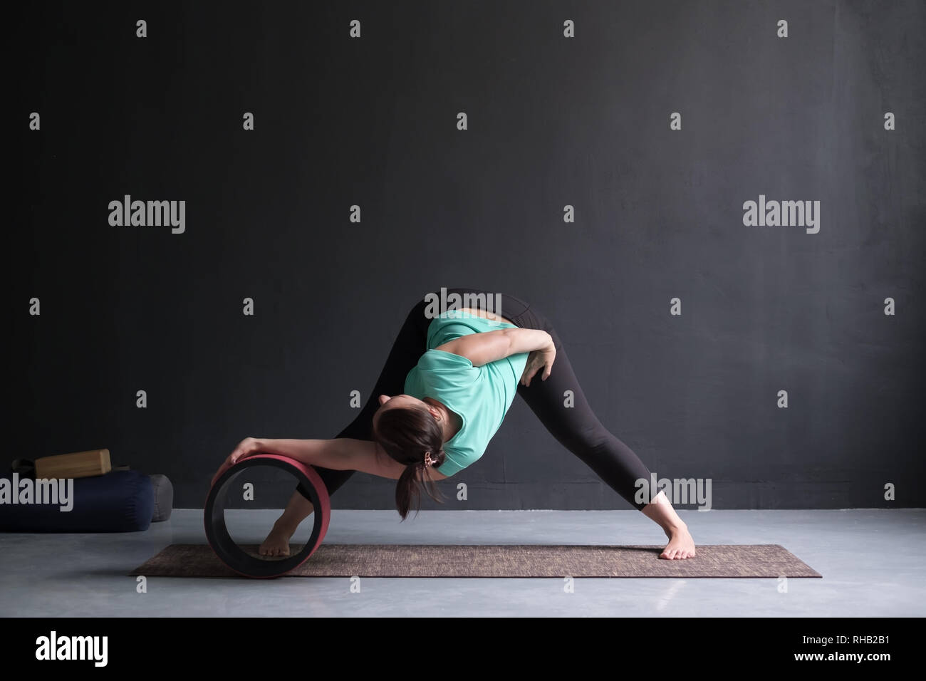 Woman doing yoga asana Wide Legged Forward Bend using special wheel ...