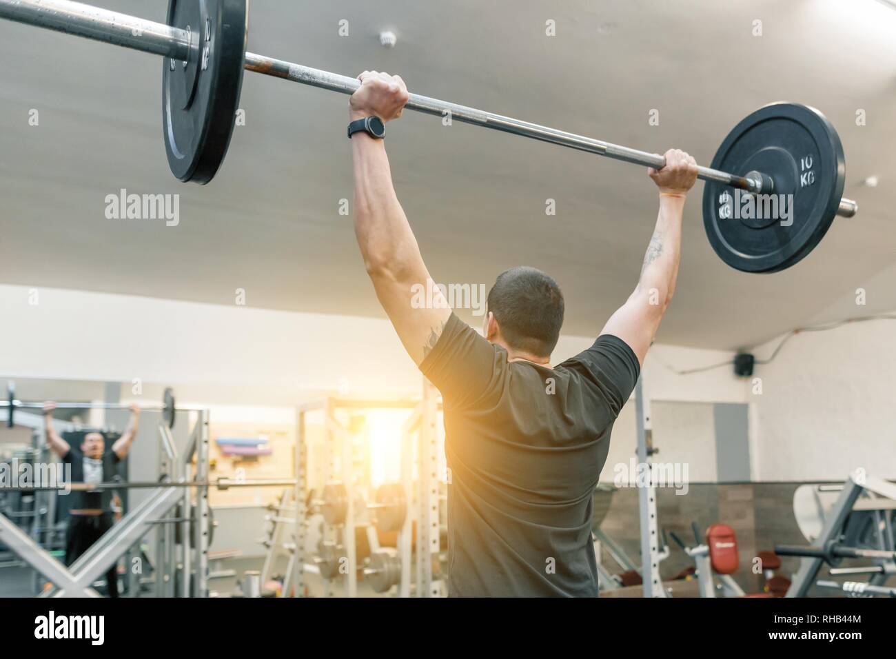 Muscular young man working with barbell heavy weights in training gym ...