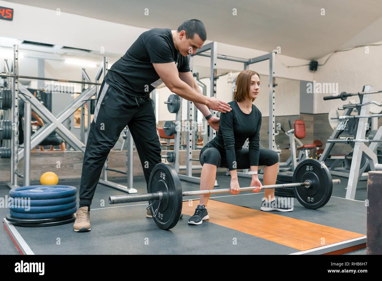 Male personal fitness trainer helping young woman to do workout in gym ...