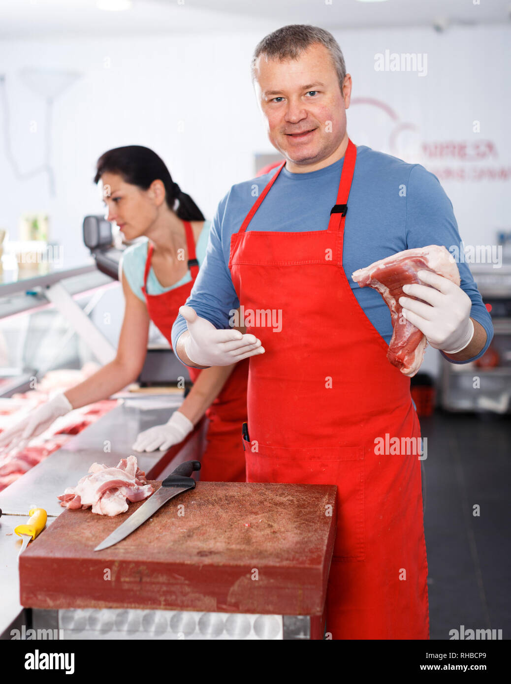 Smiling man and woman sellers working in butcher’s shop, man ...