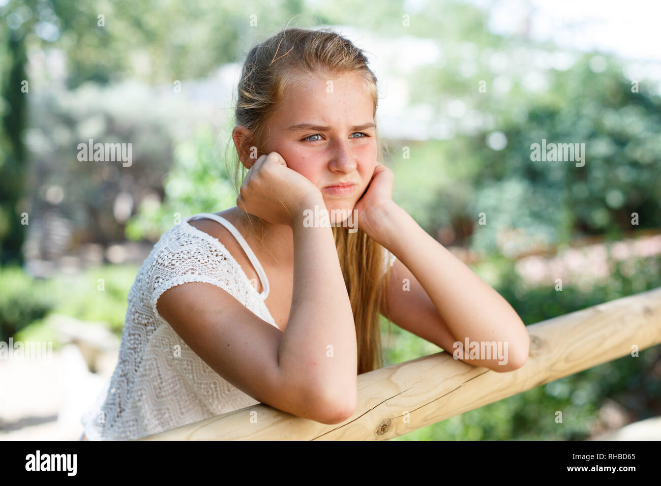 Teenage sad girl standing near fence in green park at sunny day outdoor ...
