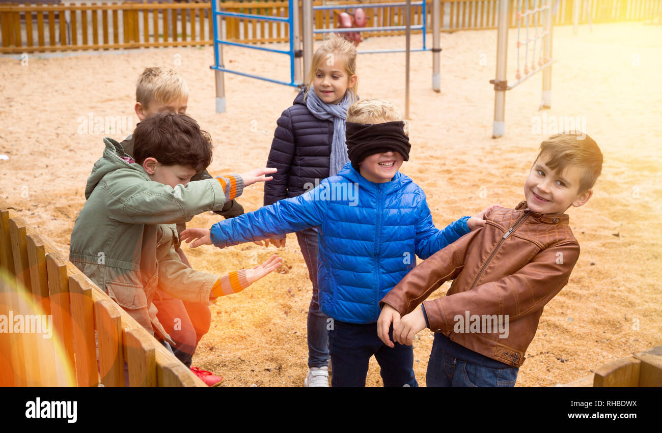 Laughing blindfolded boy catching other children on playground during ...