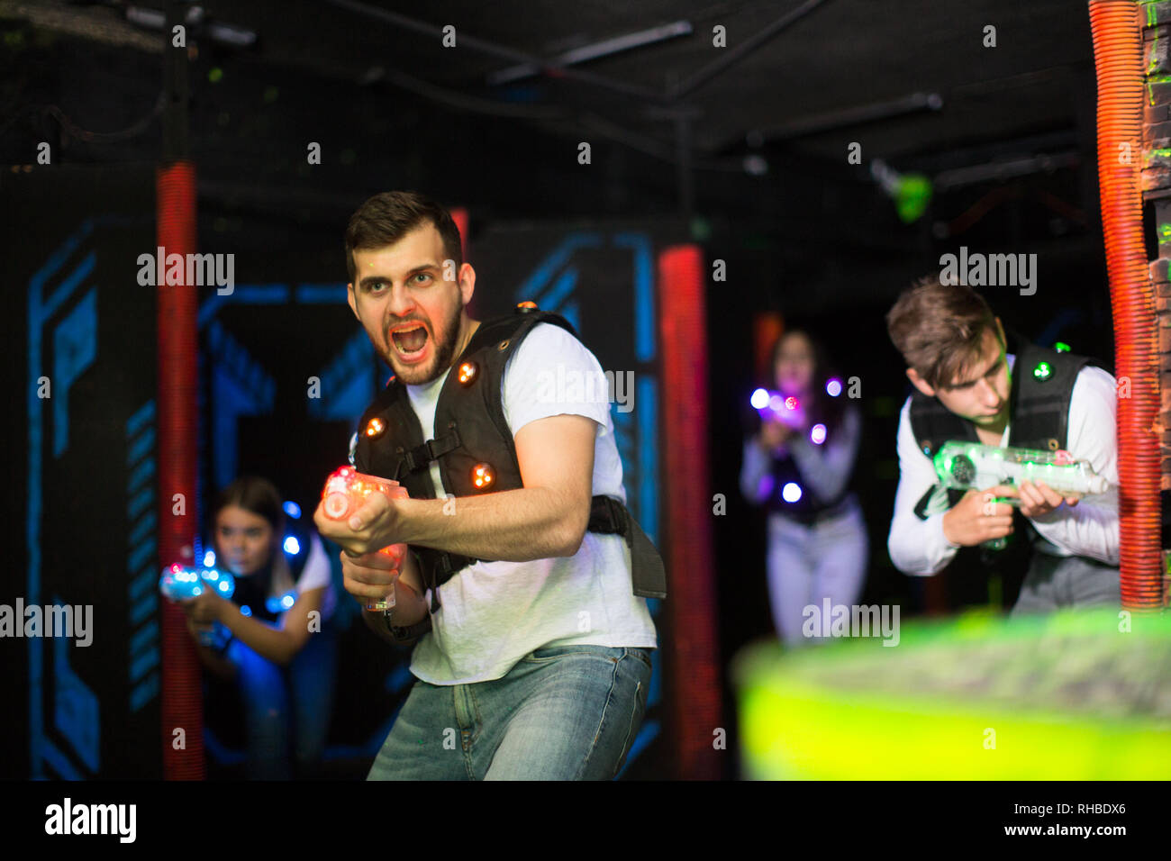 Emotional guy with laser pistol playing laser tag with friends on dark ...