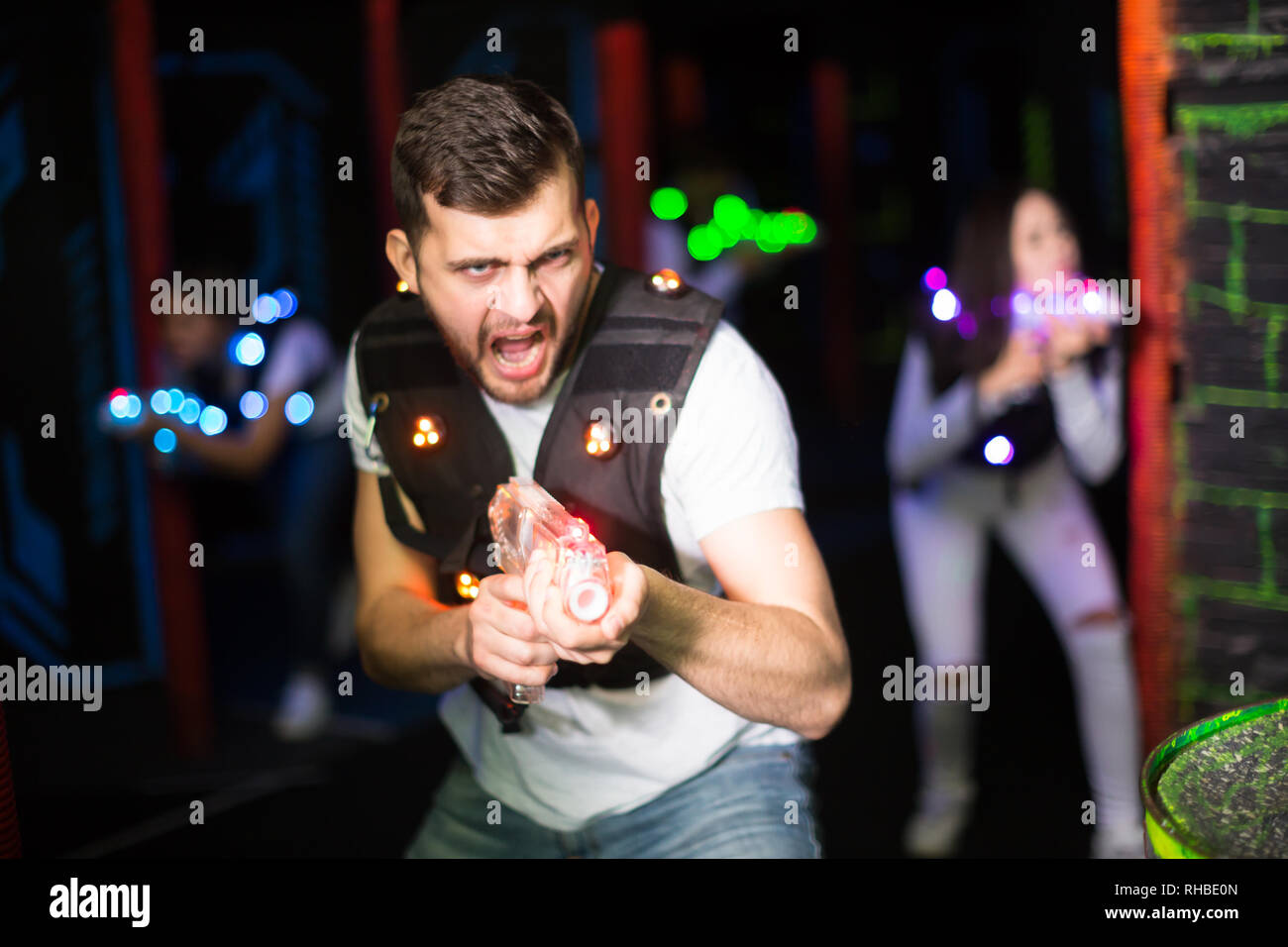 Excited guy aiming laser gun at other players during lasertag game in ...