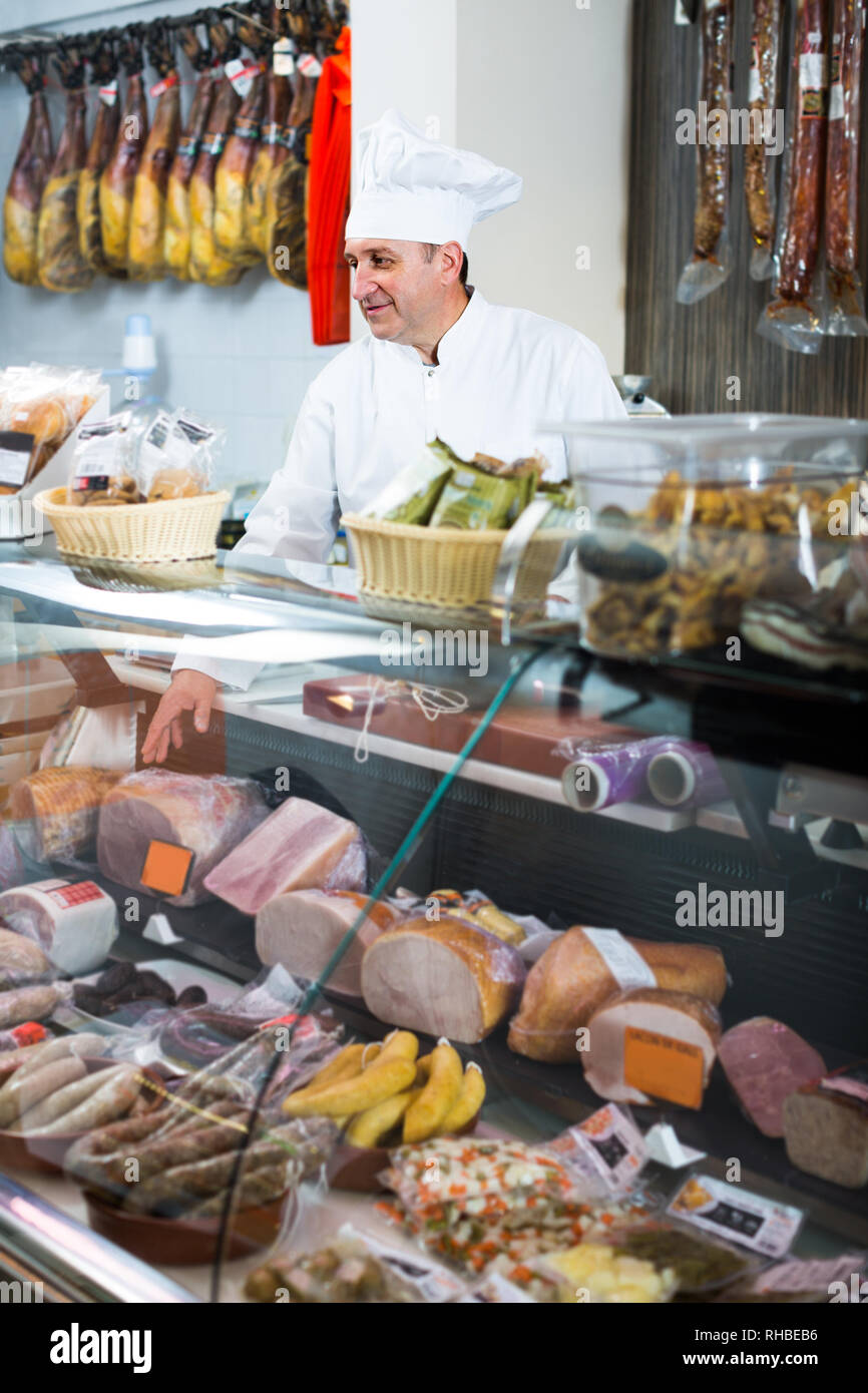 Mature male butcher with wurst and smoked meat at food counter Stock ...