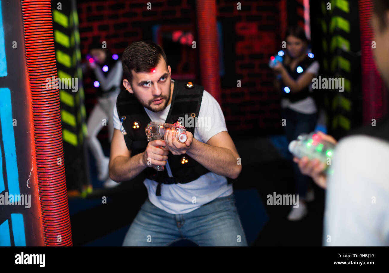 Emotional guy with laser pistol playing laser tag with friends on dark ...
