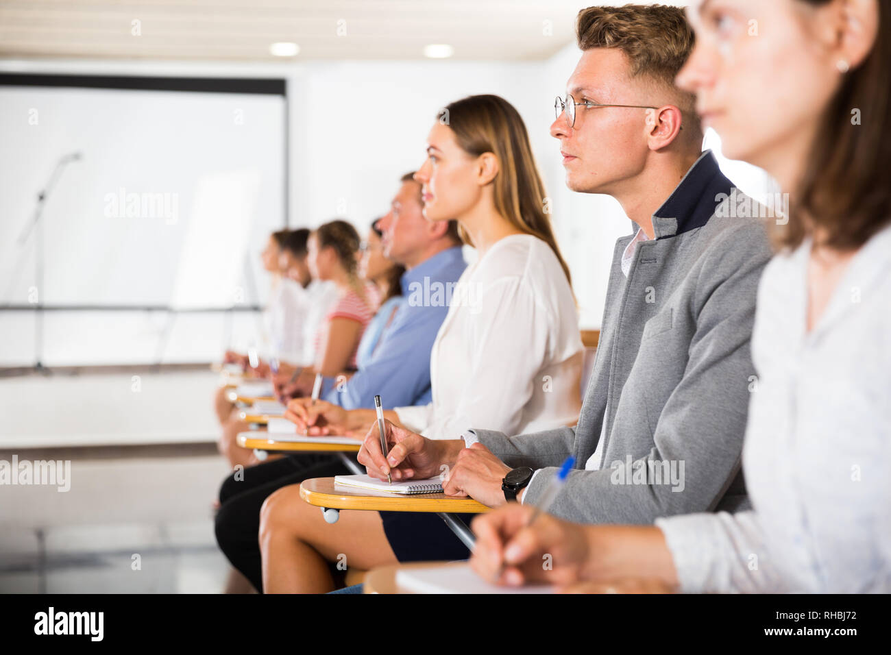 Side view of row of people listening lecturer and making notes at ...