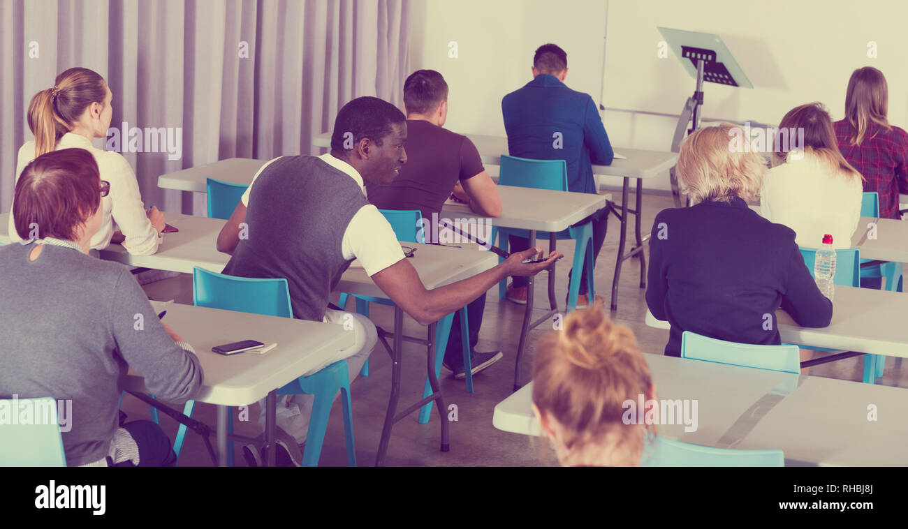 Back view of multinational group of adult students working in classroom ...