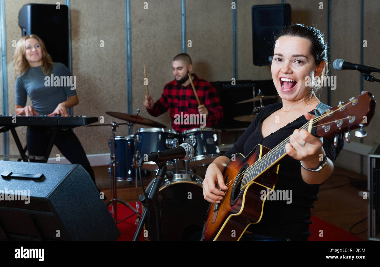 Attractive cheerful female soloist playing guitar and singing with her ...