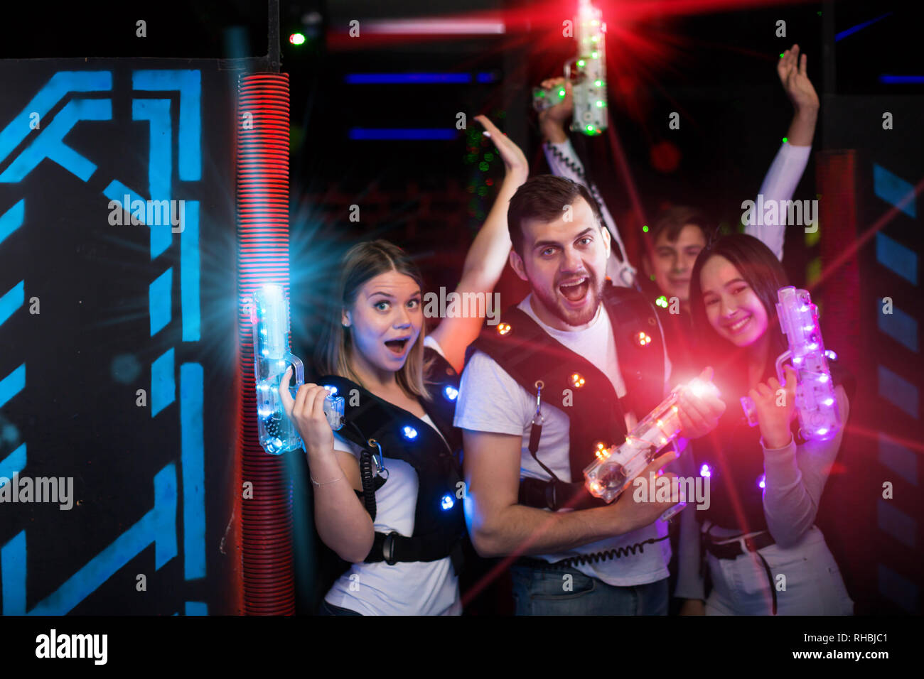 Happy young people with laser pistols posing together in bright beams ...