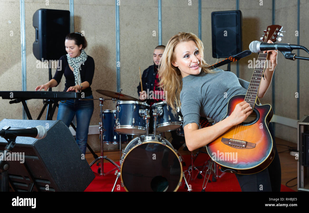 Attractive pleasant cheerful female soloist playing guitar and singing ...