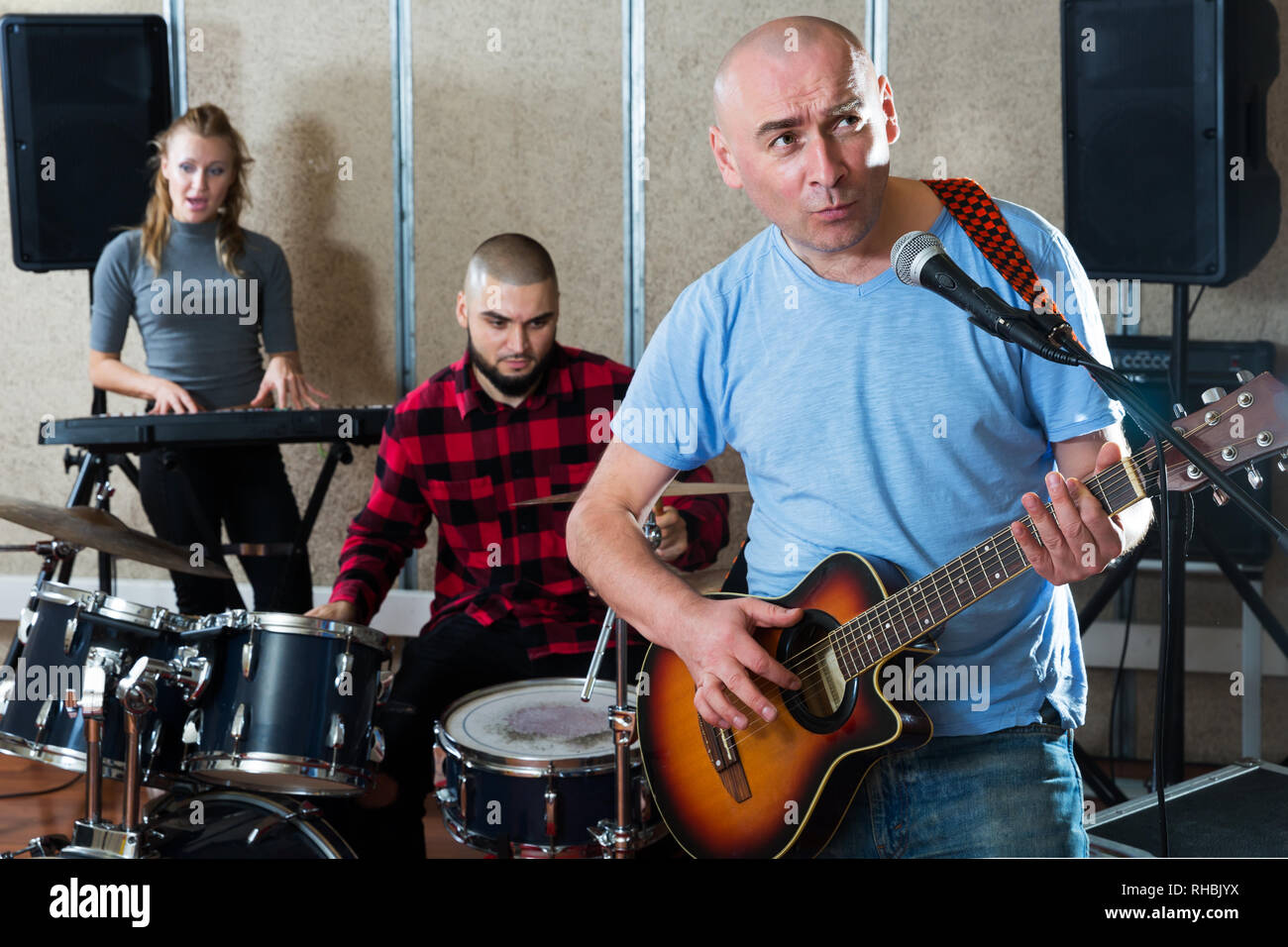 Male soloist playing guitar and singing with group of young musicians ...