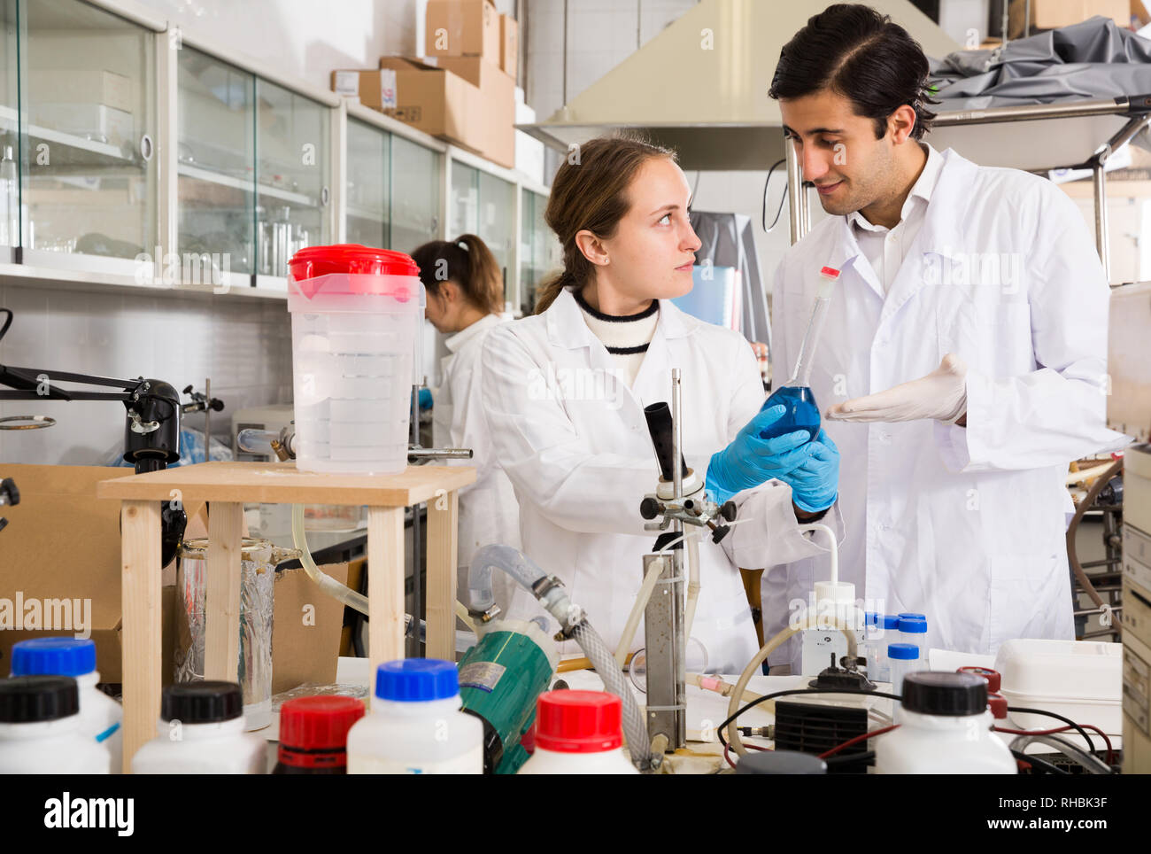Two young lab technicians discussing while working with reagents in ...