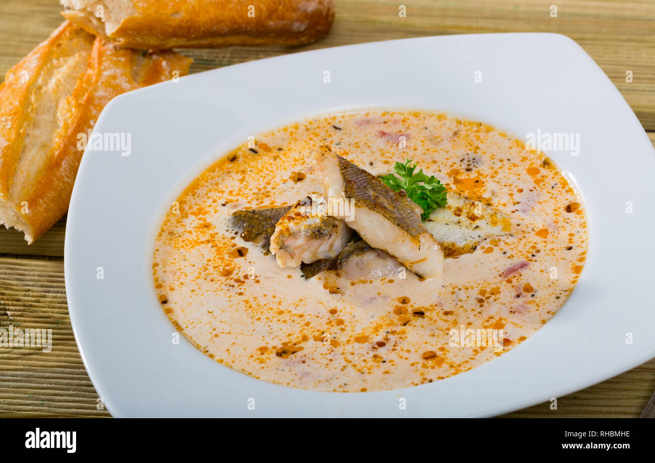 Closeup of tasty soup with white fish pollock and greens at white plate ...