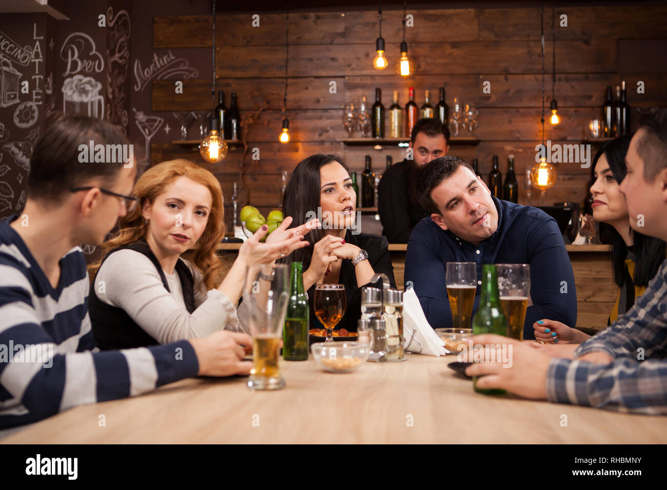 Group of young friends sitting around table in bar togethe. Cheerful ...