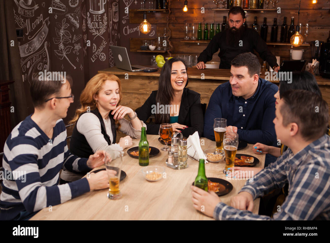 Group of young friends sitting around table in bar togethe. Cheerful ...
