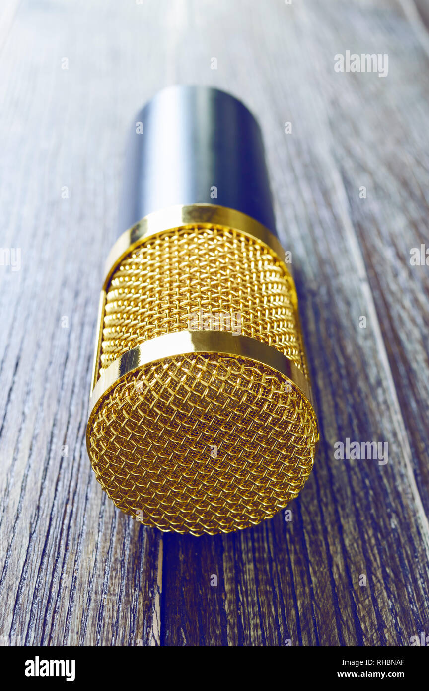 Condenser gold microphone on a wooden table. The light from left side ...