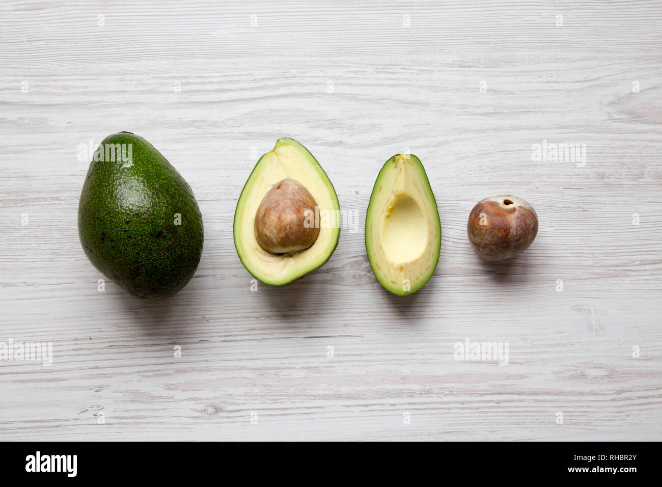 Whole and chopped avocados on white wooden background, overhead view ...