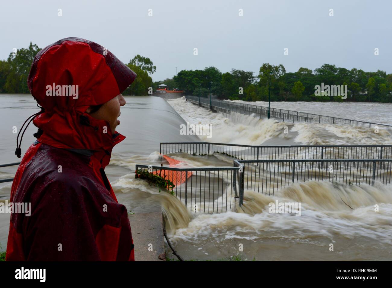 A woman in a red rain jacket holding an umbrella looks at ross river ...