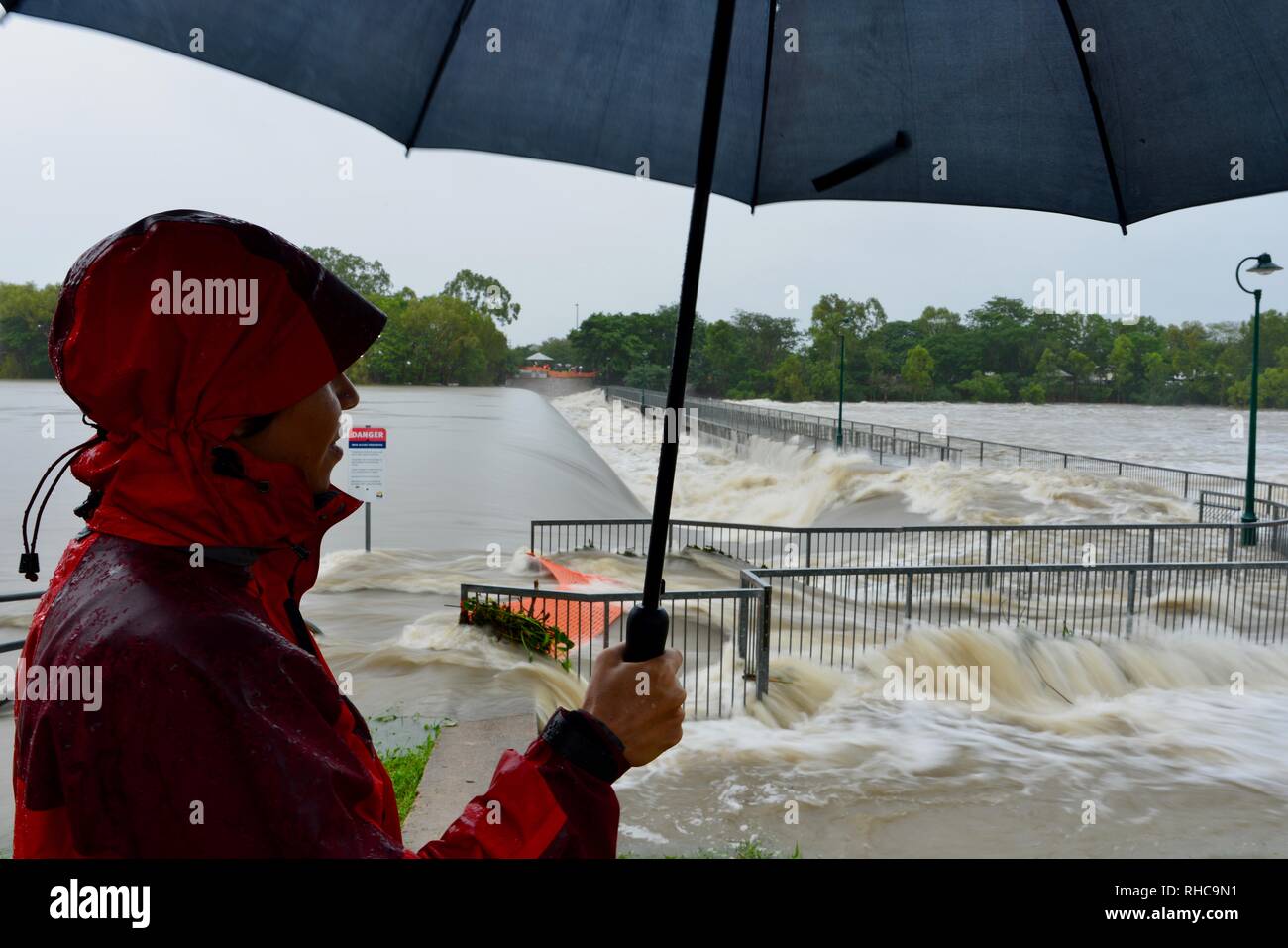 A woman in a red rain jacket holding an umbrella looks at ross river ...