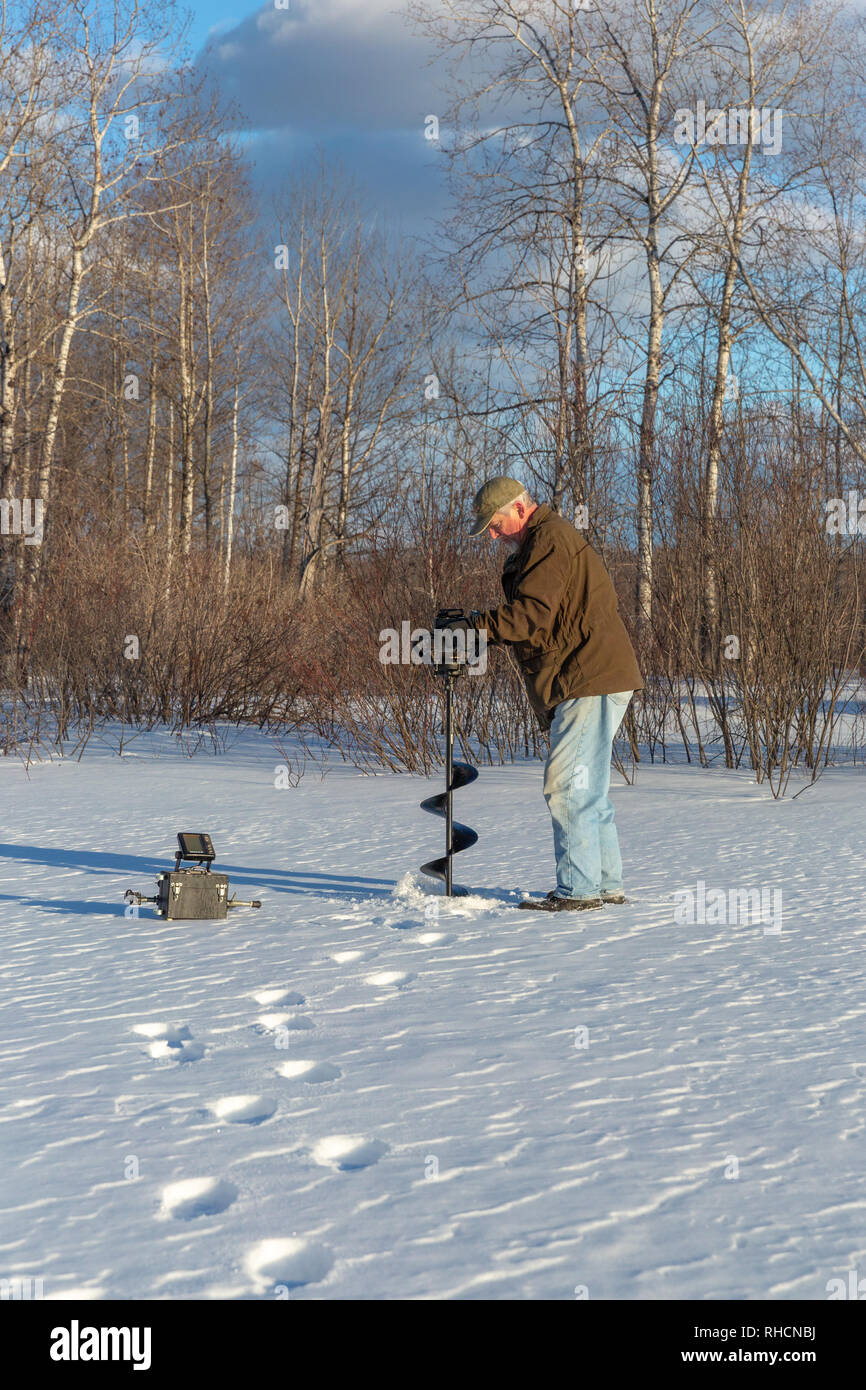 Fisherman using an ice auger to drill a hole in the ice Stock Photo - Alamy