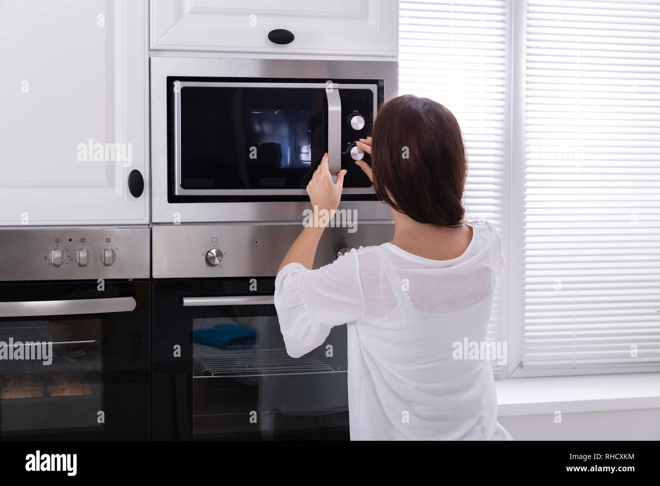 Side View Of A Young Woman Using Microwave Oven In Kitchen Stock Photo ...