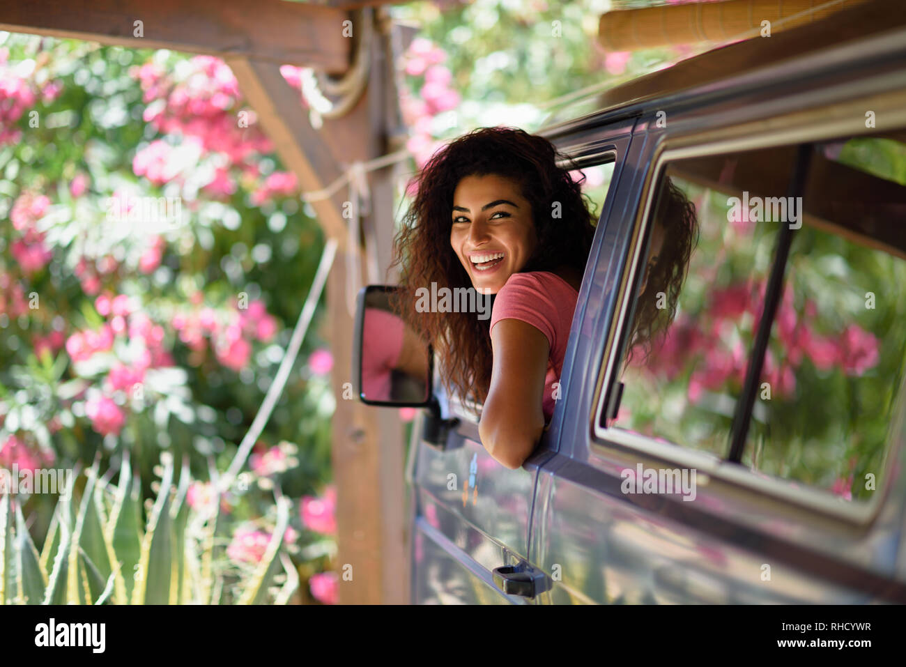 Young woman in a camper van in a beautiful camping with pink flowers ...