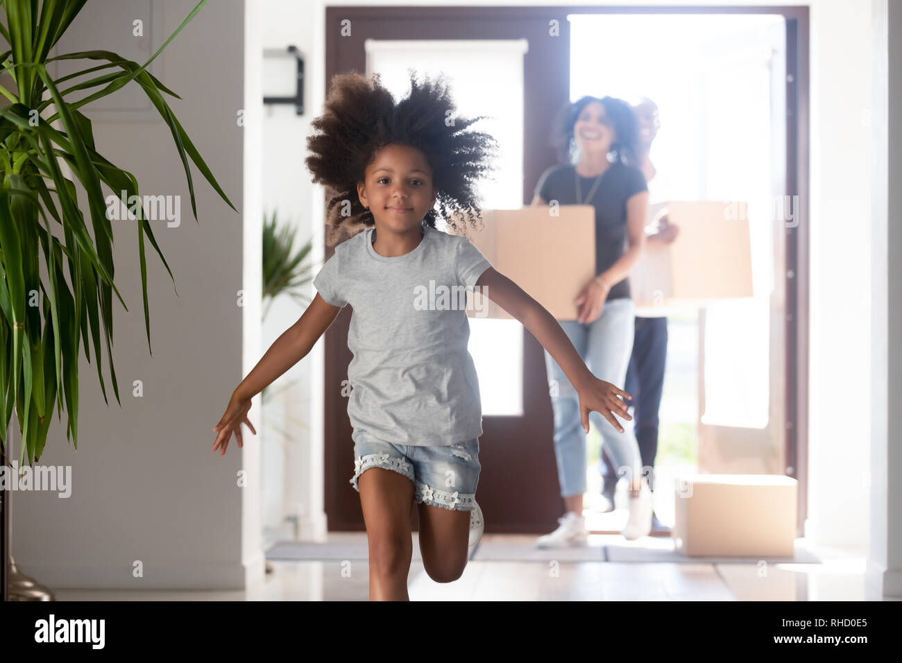 African parents entering new home with kid running in hallway Stock ...