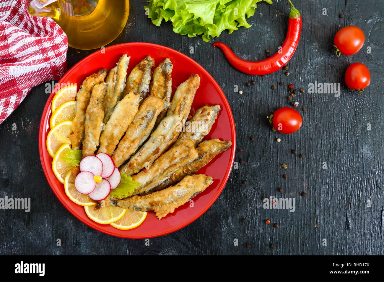 Fried capelin with lemon on a red plate on a black wooden background. A ...