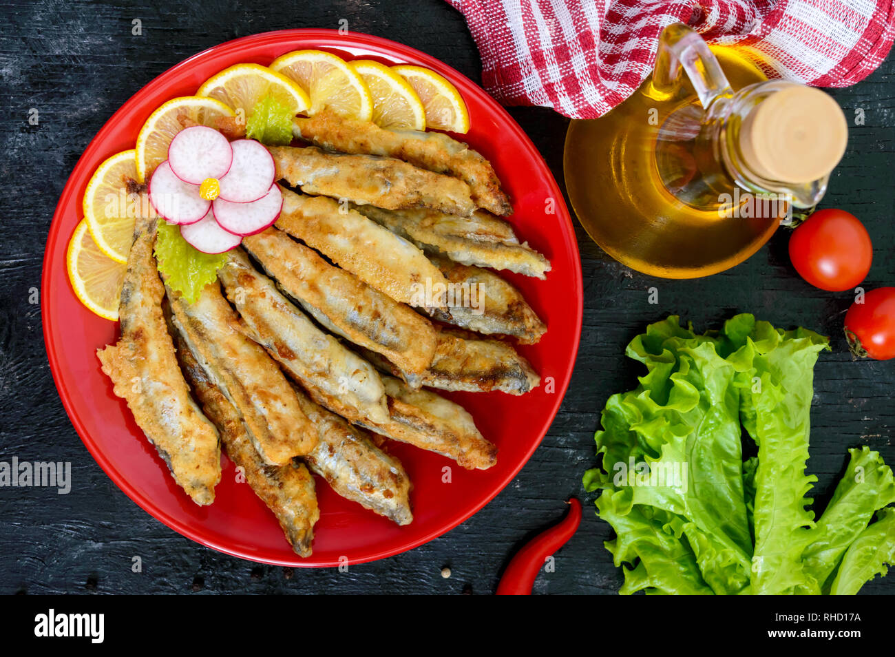 Fried capelin with lemon on a red plate on a black wooden background. A ...