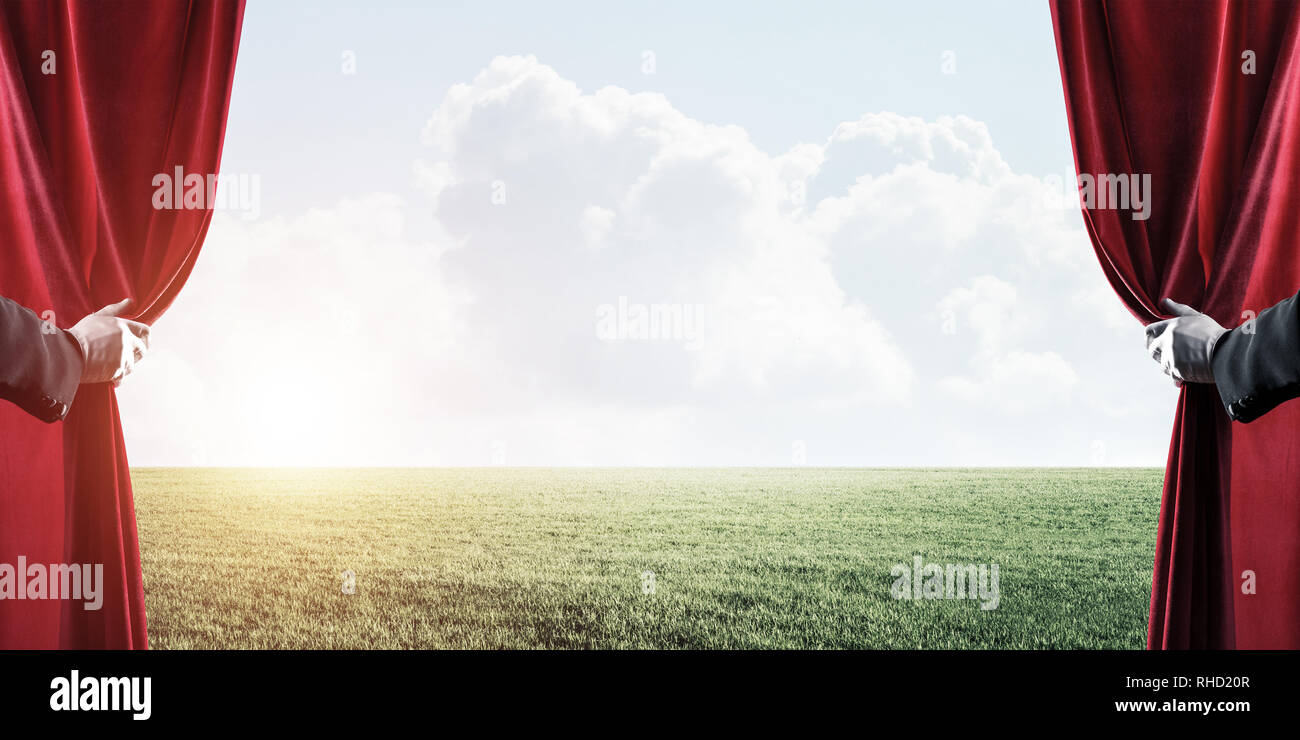 Green meadow behind red curtain and hand holding it Stock Photo - Alamy