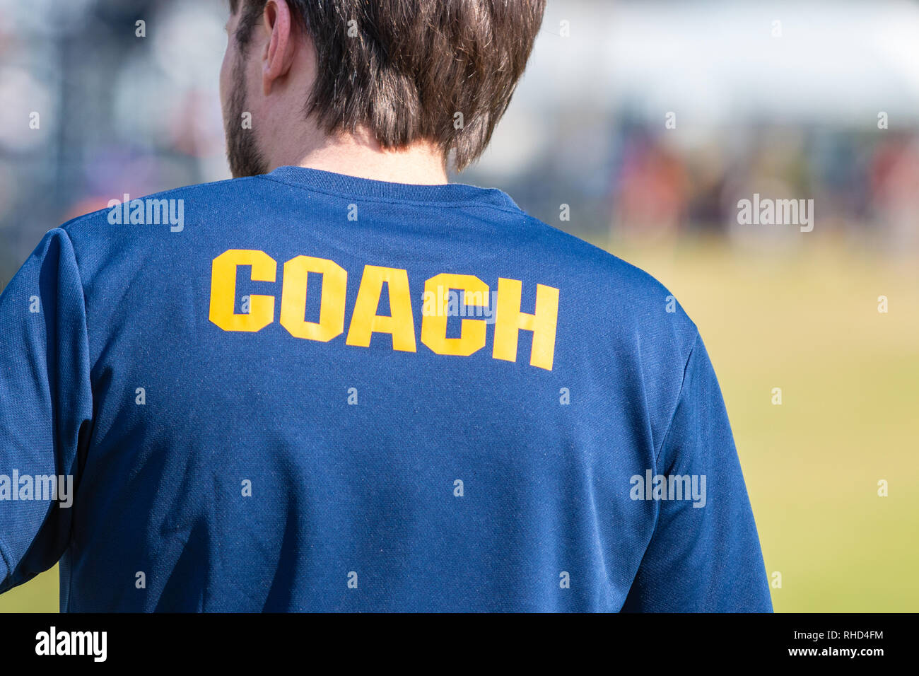 Back of male sport coach wearing blue shirt with yellow COACH word on ...