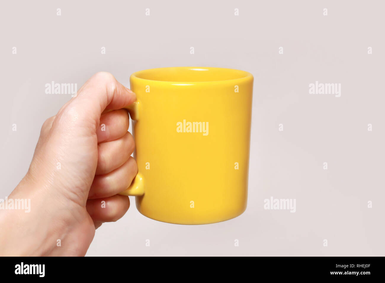 Hand holding yellow mug isolated on beige background Stock Photo - Alamy