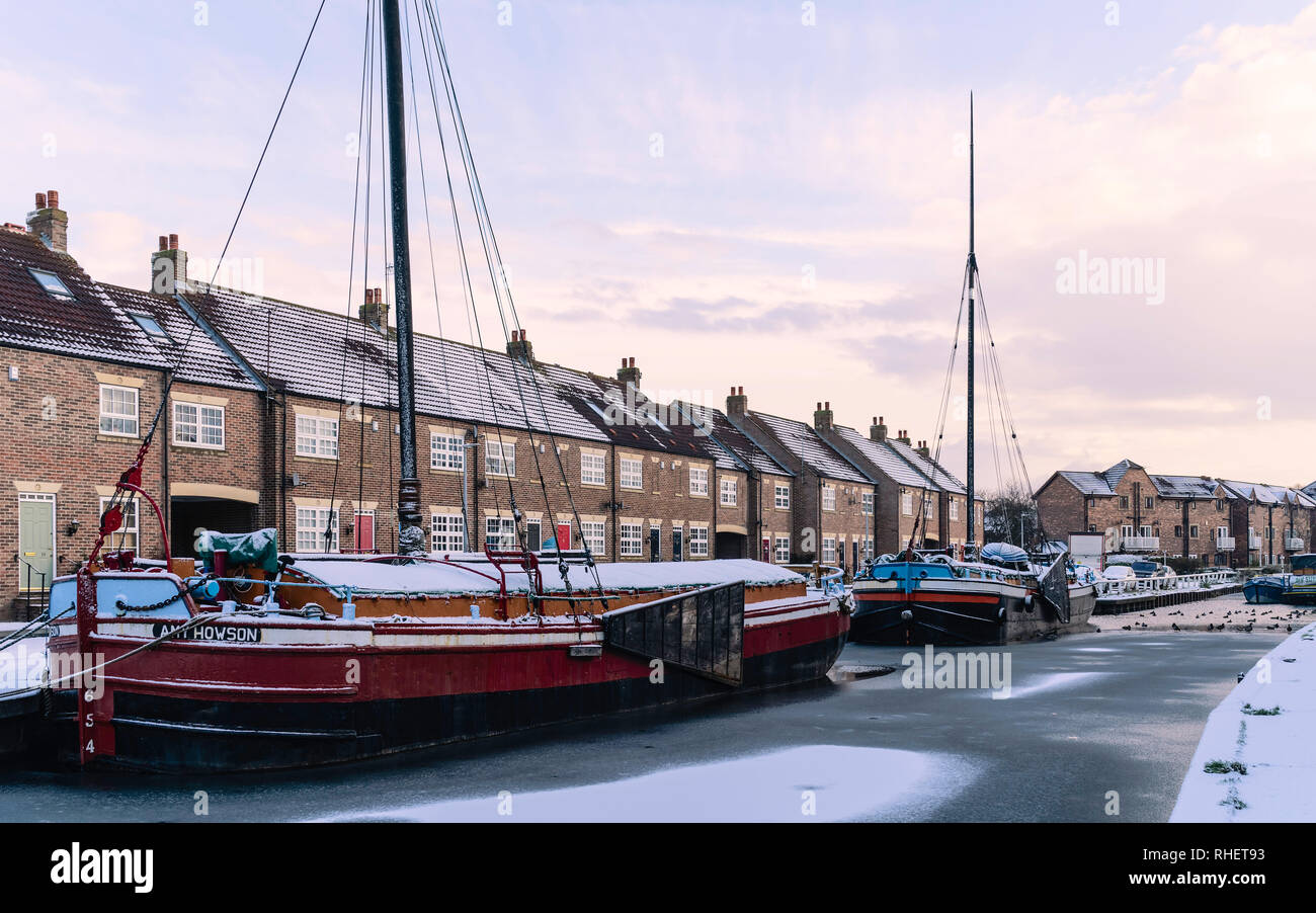 Vintage barges moored along the frozen beck (canal) and covered in snow ...