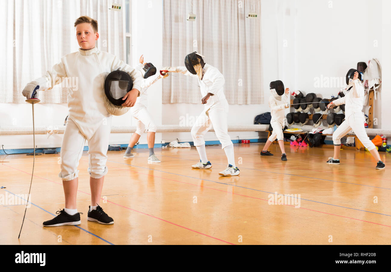 Portrait of young guy fencer posing with rapier during fencing class in ...