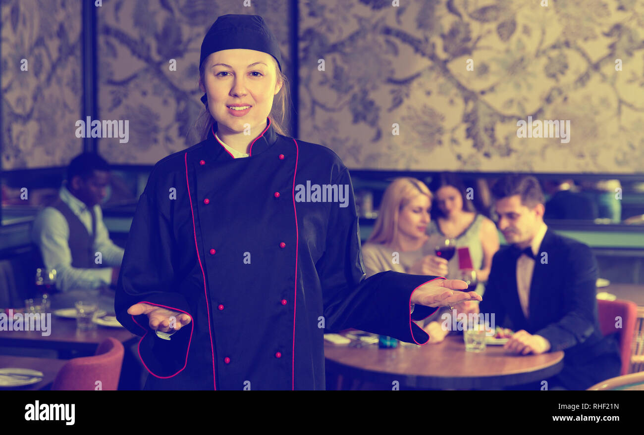 Successful young positive smiling female chef standing in restaurant ...