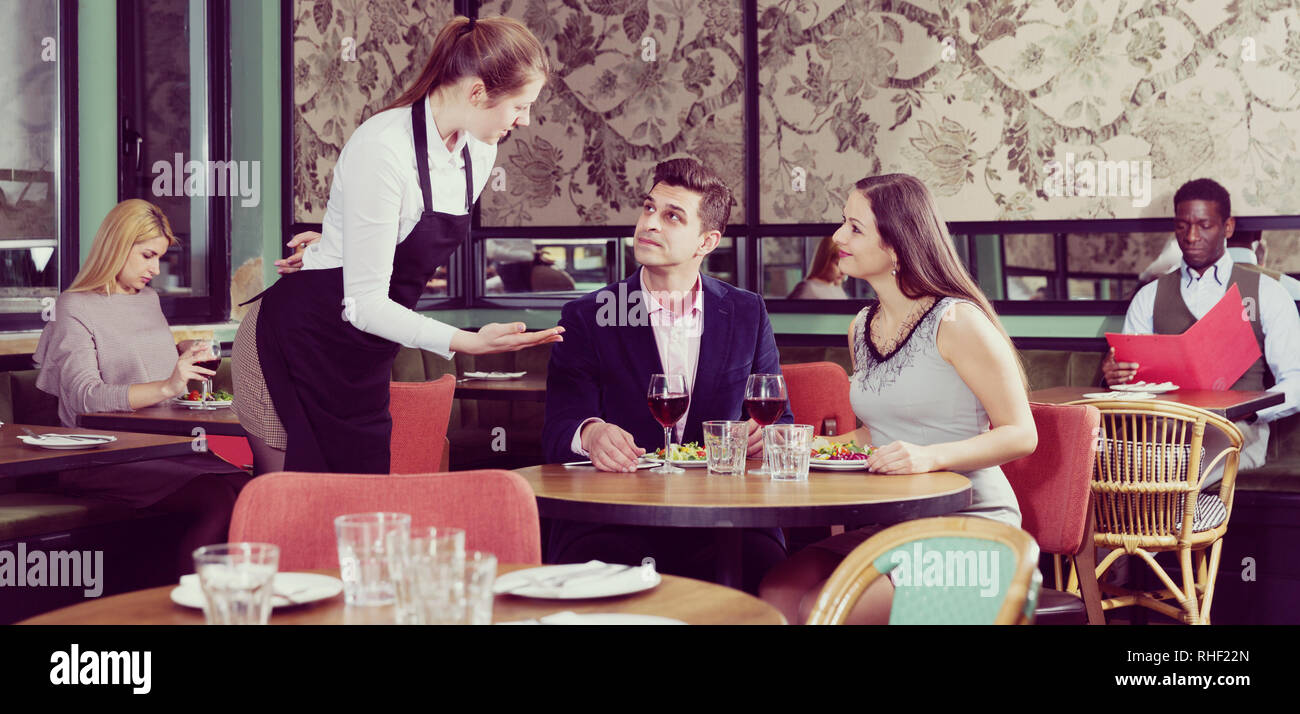 Elegant couple sitting at restaurant table talking with young waitress ...